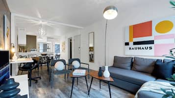 Uma sala de estar moderna com um sofá, cadeiras, um espaço de refeições e uma cozinha ao fundo.