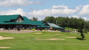 Um edifício grande com telhado verde, área de estar coberta e um gramado bem cuidado com bunkers de areia.