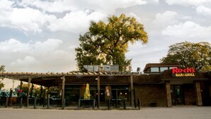Um restaurante com área de estar coberta ao ar livre, uma grande árvore e uma placa com a inscrição 'Rock's Bar & Grill'.