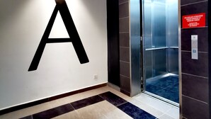 Um elevador com uma placa indicando o andar térreo, uma grande letra A iluminada na parede e uma placa de segurança vermelha.