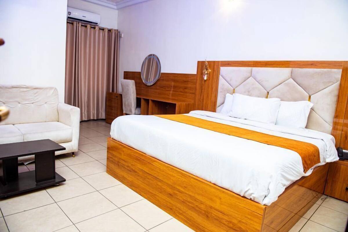 Quarto de hotel com uma cama grande, um sofá, uma mesinha e um espelho.