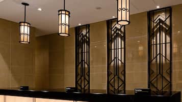 Área de recepção com parede de mármore, balcão de atendimento e três luminárias pendentes.