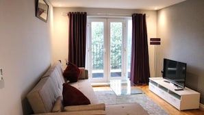 Uma sala de estar moderna com sofá, televisão e mesa de centro de vidro.