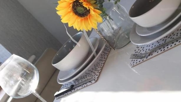 Uma mesa de jantar com um vaso de girassóis, uma taça de vinho e uma estátua de Buda ao fundo.