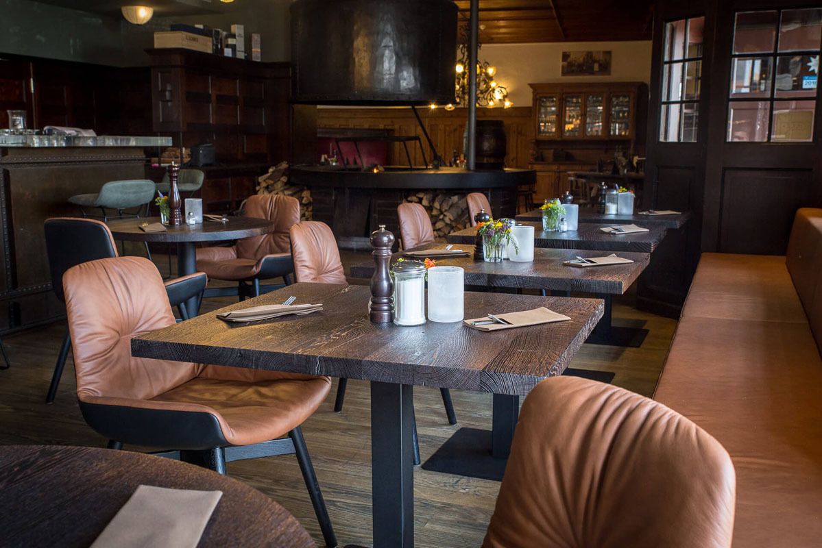 Um restaurante com mesas de madeira e cadeiras de couro, um espaço de bar e um forno preto grande ao fundo.