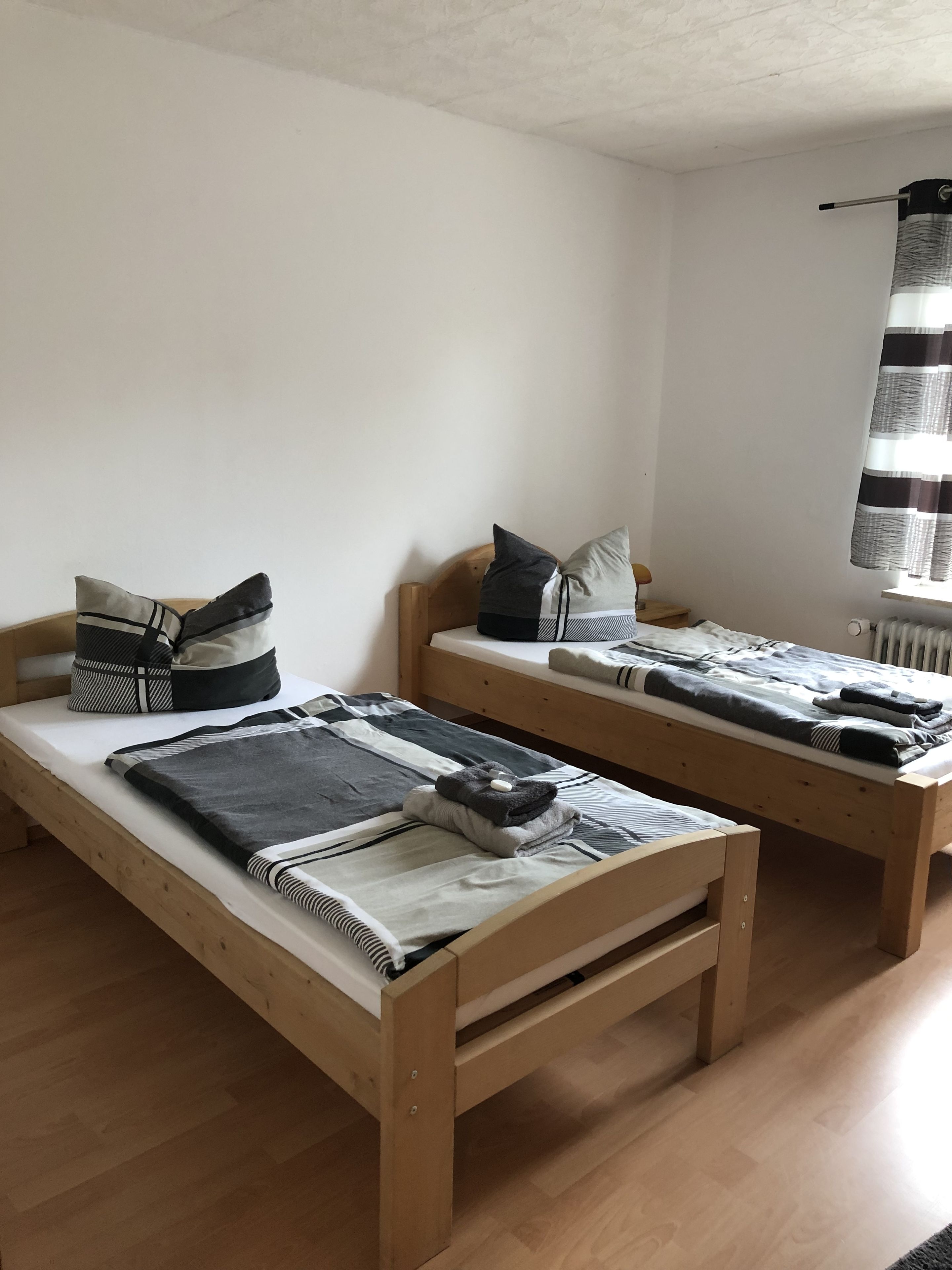 Quarto pequeno e limpo, com duas camas de madeira, cada uma com travesseiro e cobertor.