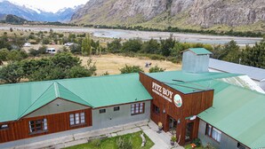Uma pousada com telhado verde, fachada de madeira e uma placa com a inscrição 'Fitz Roy Hostería de Montaña'.