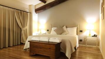 Quarto com piso de madeira, cama com roupa de cama branca, duas luminárias de cabeceira e um banco de madeira.