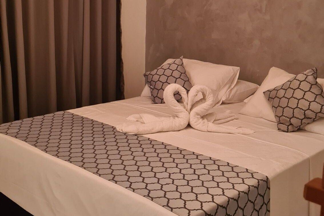 Cama arrumada com um edredom estampado e duas toalhas dobradas em formato de cisne.