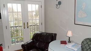 Um quarto com uma poltrona de couro preto, uma mesa redonda pequena com uma luminária, um livro vermelho e um mapa.