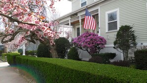 Uma casa de dois andares com um jardim da frente bem cuidado, uma bandeira e uma placa com a inscrição 'Windsome'.