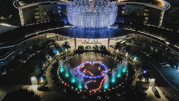 Um edifício com vários níveis, átrio central, fachada de vidro ampla e uma fonte com luzes coloridas.