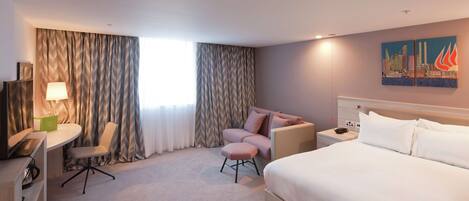 Quarto de hotel com cama, escrivaninha com cadeira, sofá e um quadro na parede.
