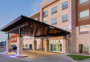 Entrada de hotel com galeria coberta, colunas de pedra e porta de vidro.