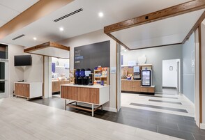 Interior moderno de uma cafeteria com balcão de café, área de estar e painel de menu digital.
