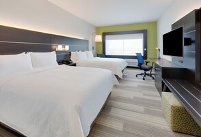 Quarto de hotel com duas camas, uma escrivaninha com cadeira, TV de tela plana e janela com vista para a cidade.