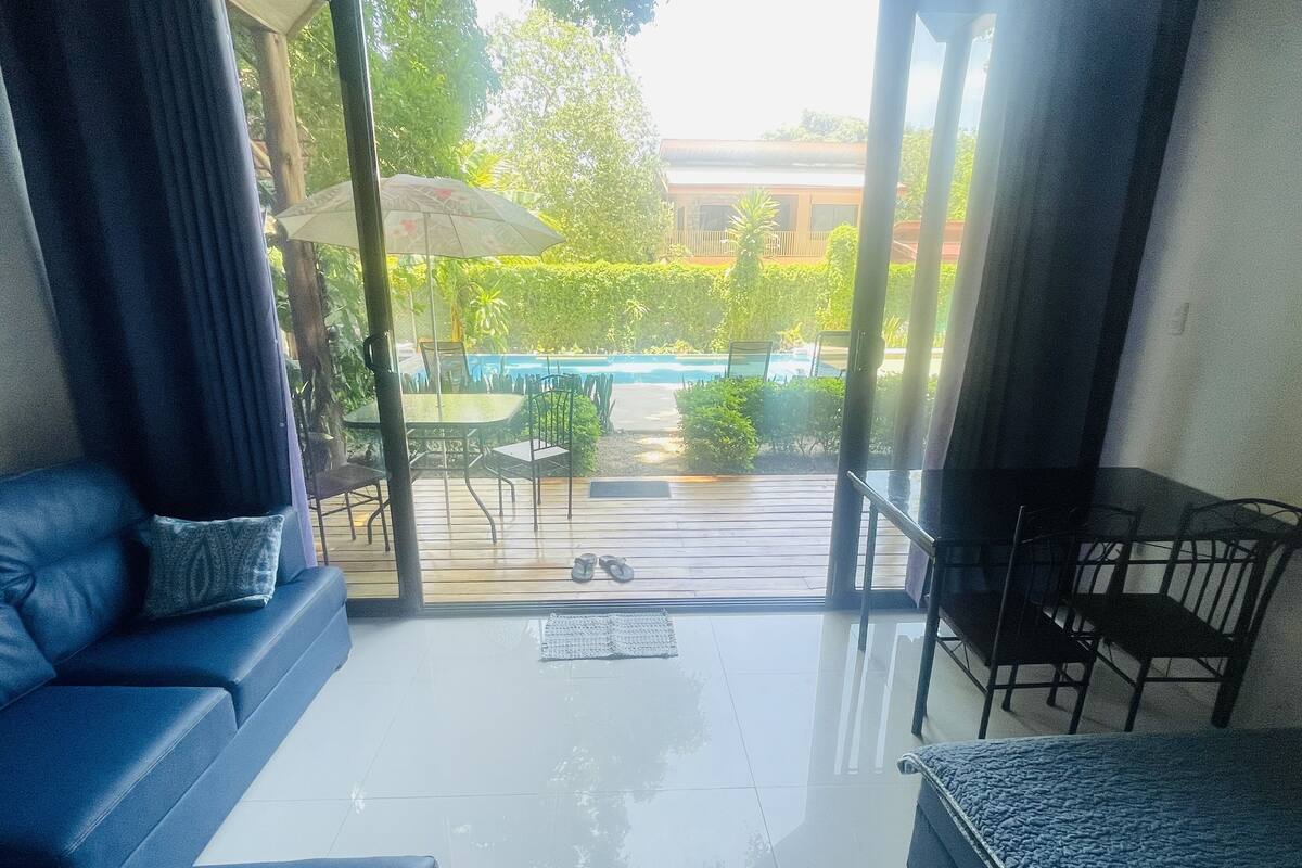 Uma sala de estar moderna com um sofá azul, uma mesinha e vista para uma piscina e jardim através de grandes janelas.