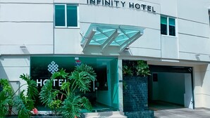 Entrada do Infinity Hotel com design moderno, incluindo uma cobertura de vidro e uma placa.