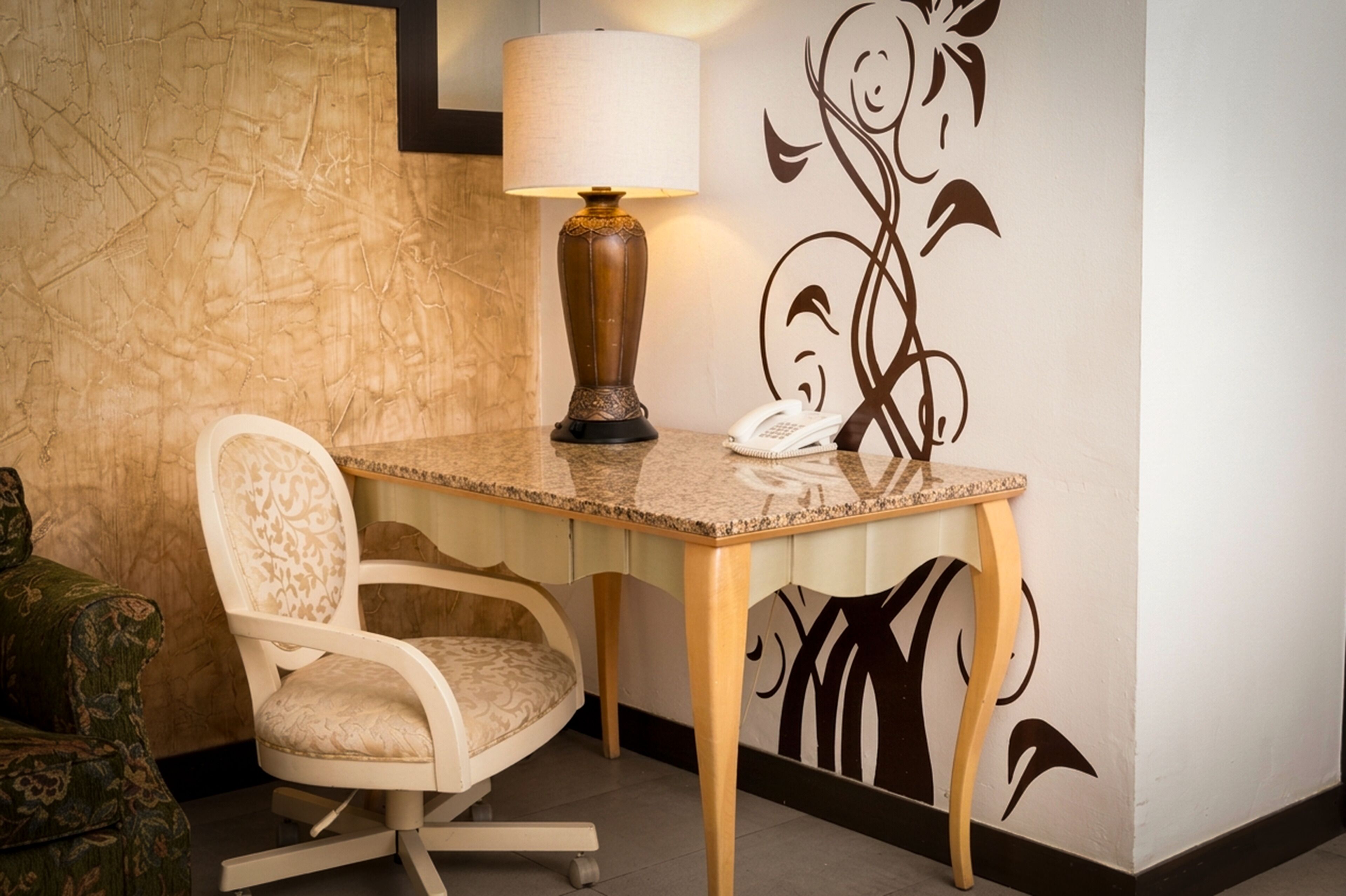 Quarto com escrivaninha, cadeira, abajur e parede com padrão floral.
