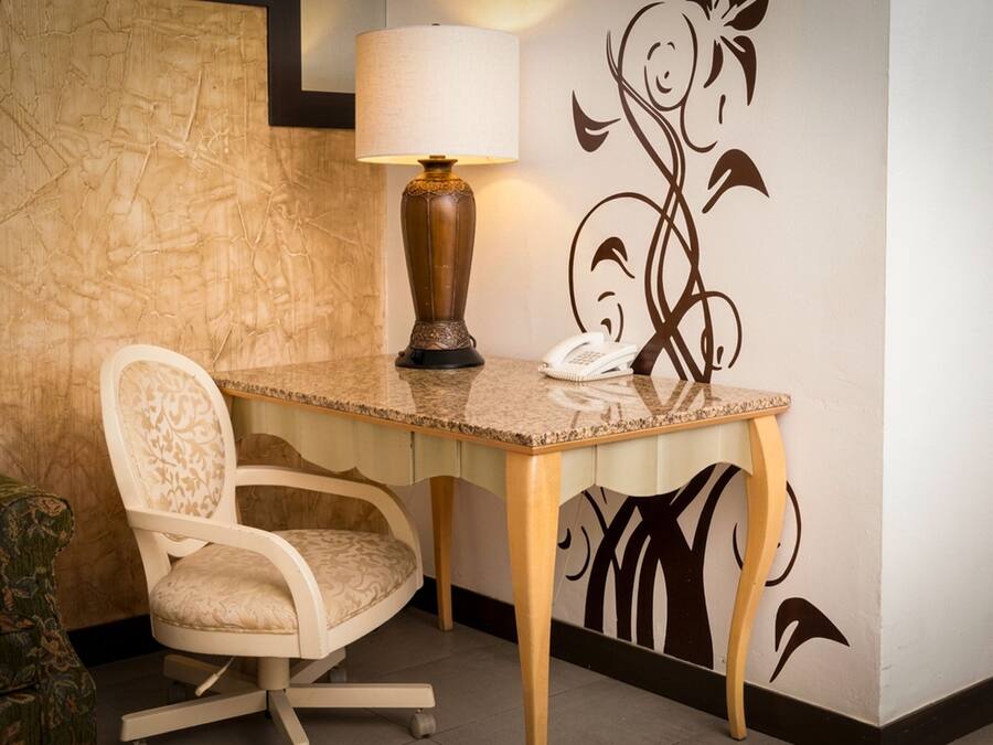 Quarto com escrivaninha, cadeira, abajur e parede com padrão floral.