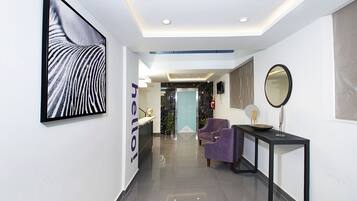 Um hall de hotel moderno com balcão de recepção, assentos roxos, uma grande obra de arte emoldurada e uma placa que diz “hello”.