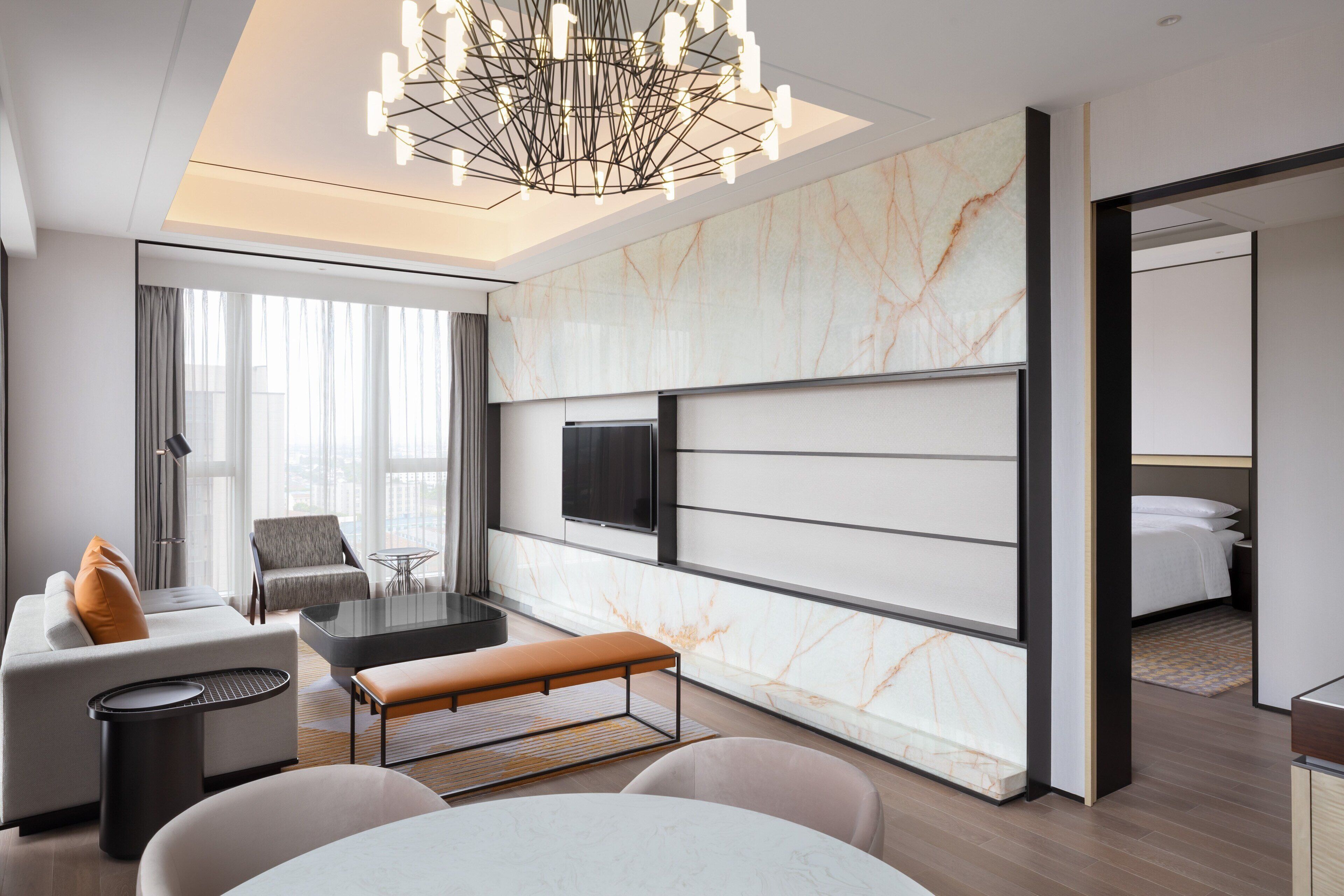 Quarto de hotel moderno com uma televisão grande, um sofá, uma mesa de jantar e um banco.