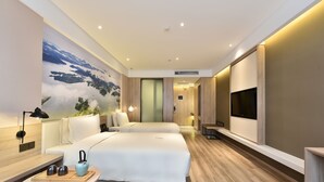 Quarto de hotel moderno com uma cama grande, televisão, escrivaninha com abajur e um mural na parede.