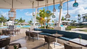 Pátio de resort com mobiliário de exterior, mesas e luminárias pendentes.