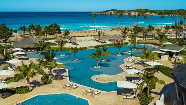 Um resort com várias piscinas, palmeiras e vista para a praia.