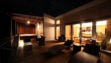 Uma área externa ampla com deck de madeira, espaço de estar com móveis de vime e vista para o céu noturno.