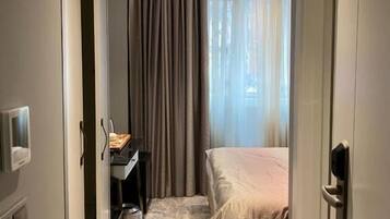 Quarto de hotel com cama, escrivaninha, guarda-roupa e banheiro.
