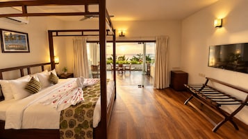 Quarto de hotel com cama de dossel, televisão de tela plana, um banco de madeira e varanda com vista para o oceano.