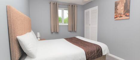 Quarto com cama, cortinas, janela, luminária na parede e quadro emoldurado.