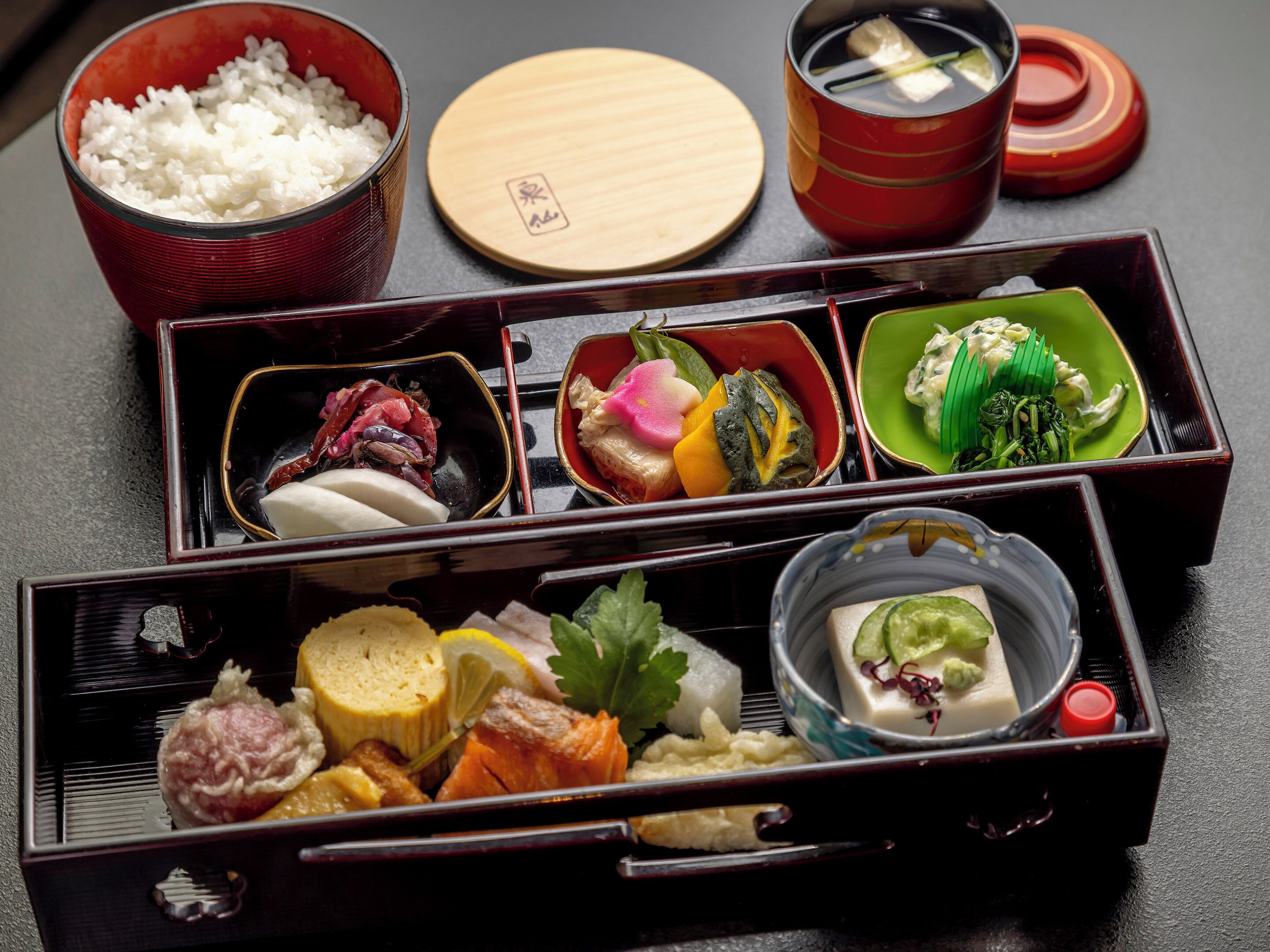 Uma bento japonesa tradicional com diversos alimentos, incluindo arroz, peixe, legumes e tofu.