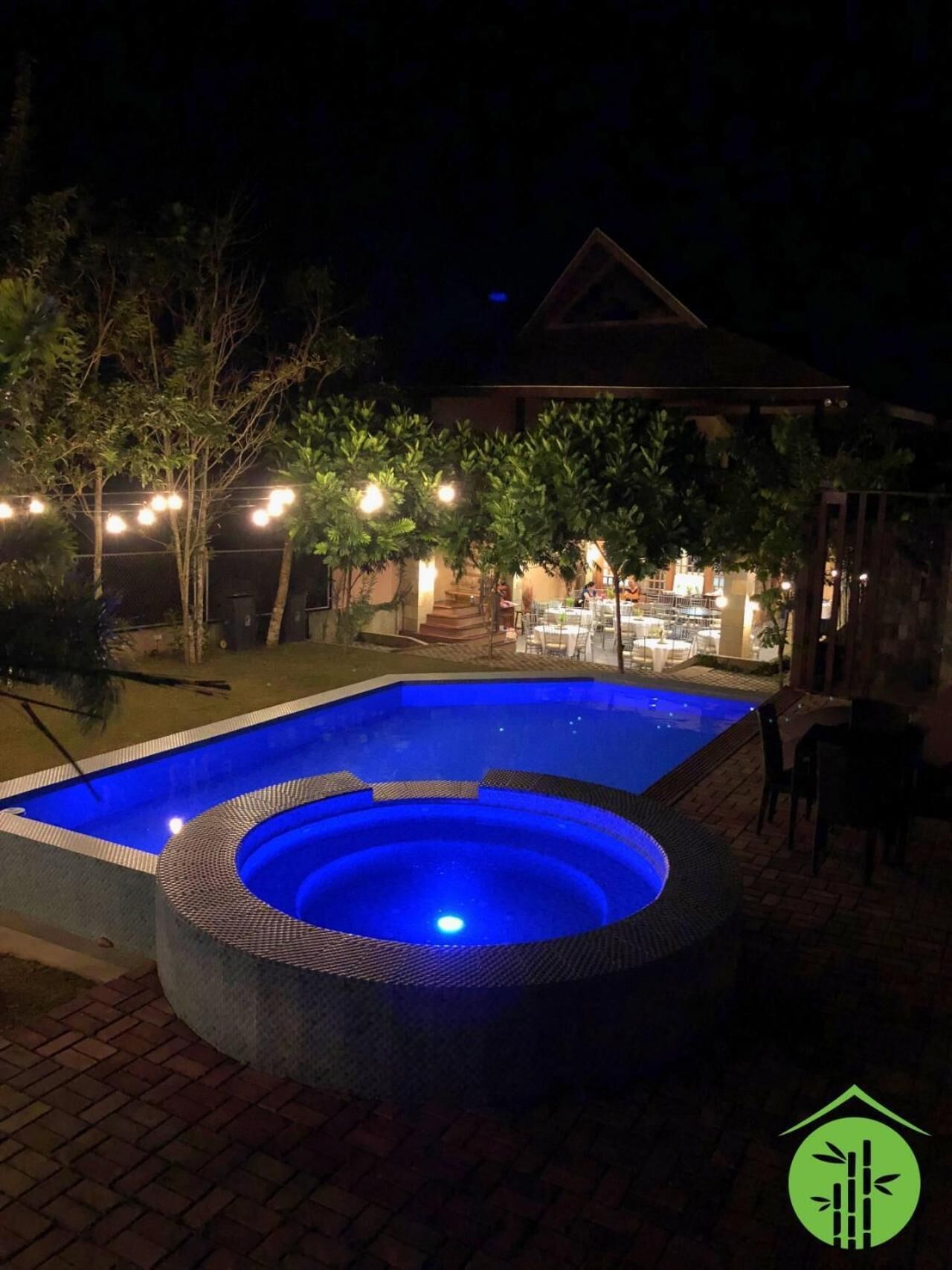 Piscina com hidromassagem, cercada por um terraço de tijolos e árvores.