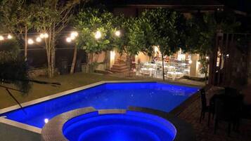 Piscina com hidromassagem, cercada por um terraço de tijolos e árvores.