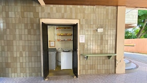 Uma entrada coberta com paredes e chão de azulejos, que dá acesso a um espaço com máquina de lavar roupa e uma pequena prateleira.