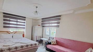 Quarto com uma cama, um sofá rosa, uma escrivaninha e uma janela com cortinas estampadas.