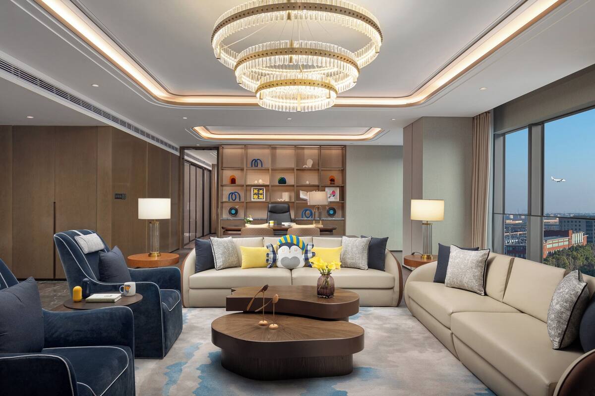 Um hall de hotel moderno com um lustre grande, um conjunto de sofás, uma mesa de centro e uma estante de livros.