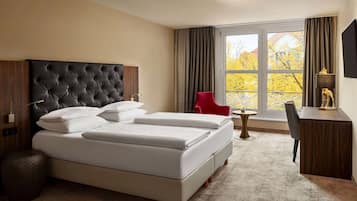 Quarto de hotel com uma cama grande, uma mesa, uma cadeira e uma janela com cortinas.