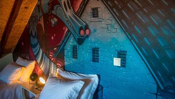 Um quarto com uma cama, um mural na parede com desenho de uma casa e uma pequena janela.