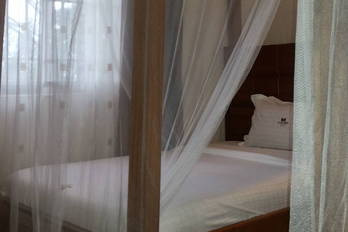 Uma cama com dossel e colunas, estrutura de madeira e roupa de cama branca.