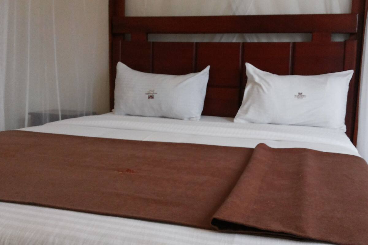 Quarto de hotel com uma cama grande, cabeceira de madeira e roupa de cama branca.