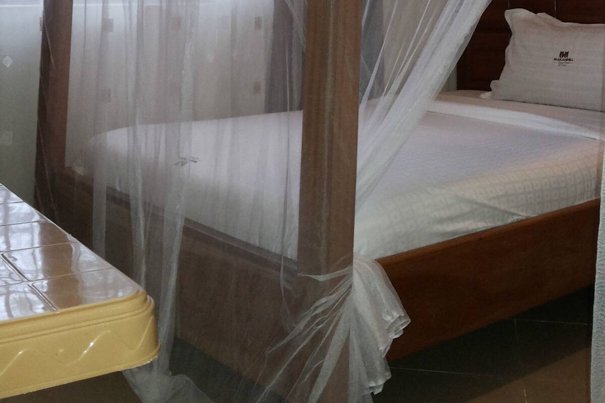 Uma cama de dossel com estrutura de madeira e cortina translúcida.