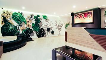 Um lobby moderno com um grande mural na parede retratando plantas tropicais, um balcão de recepção e uma escadaria.
