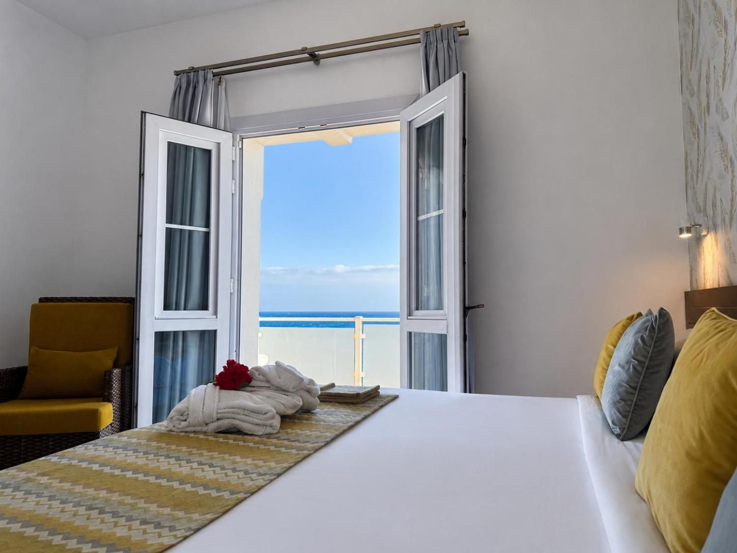 Quarto de hotel com cama, uma cadeira e vista para o mar.