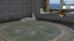 Uma banheira de hidromassagem com vista para o oceano, uma toalha e uma garrafa de champanhe em uma prateleira.