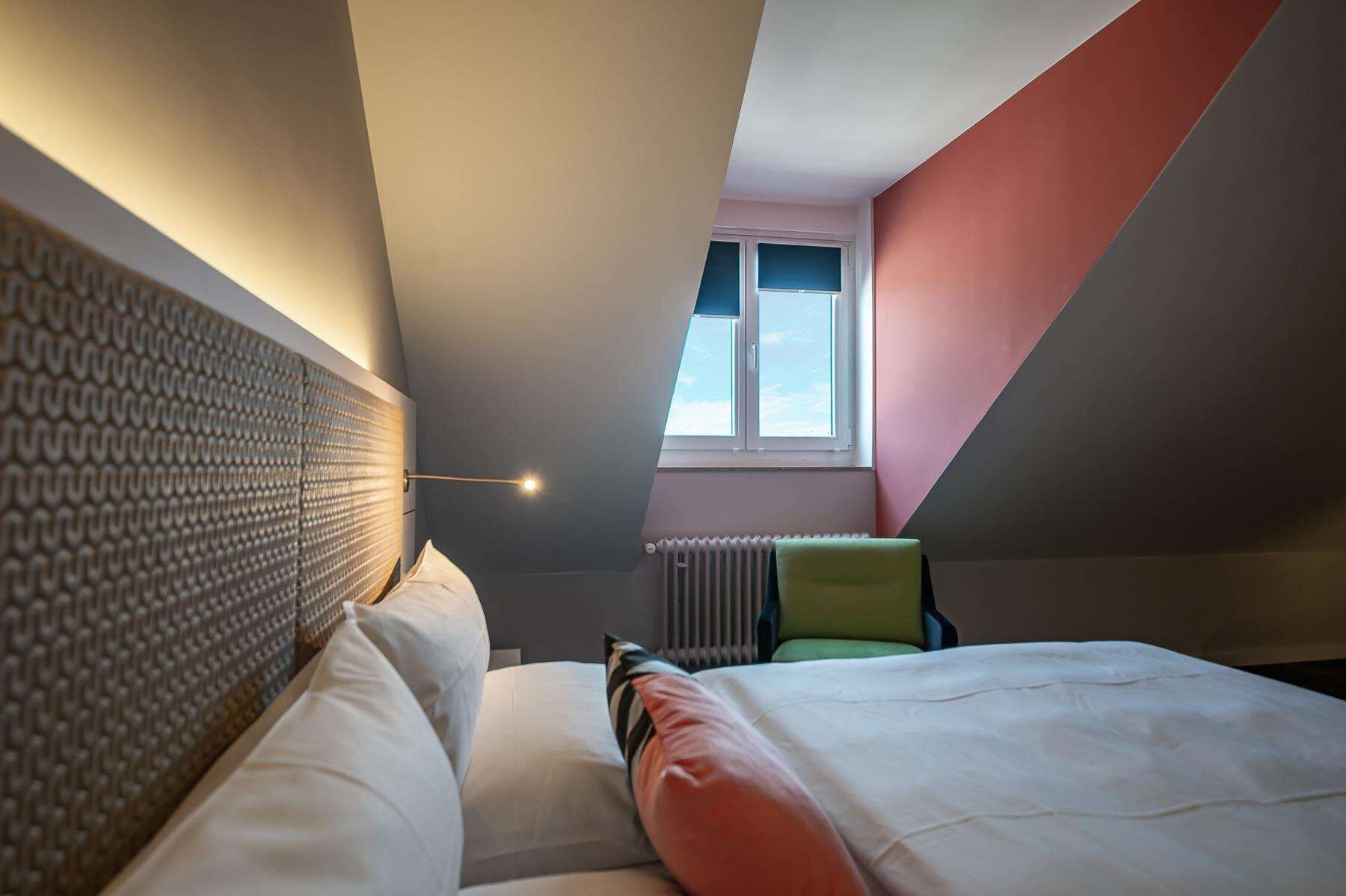 Quarto com teto inclinado, radiador, janela e cama com almofadas.