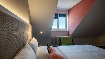 Quarto com teto inclinado, radiador, janela e cama com almofadas.