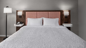 Quarto de hotel com uma cama grande, duas mesas de cabeceira, um criado-mudo, uma lâmpada e um telefone fixado na parede.